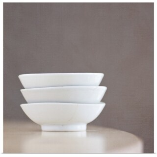"Three small white stacked bowls on light wood table against brown ...